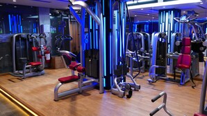 Academia moderna com diversos equipamentos de exercício, piso de madeira e iluminação em tons de azul.