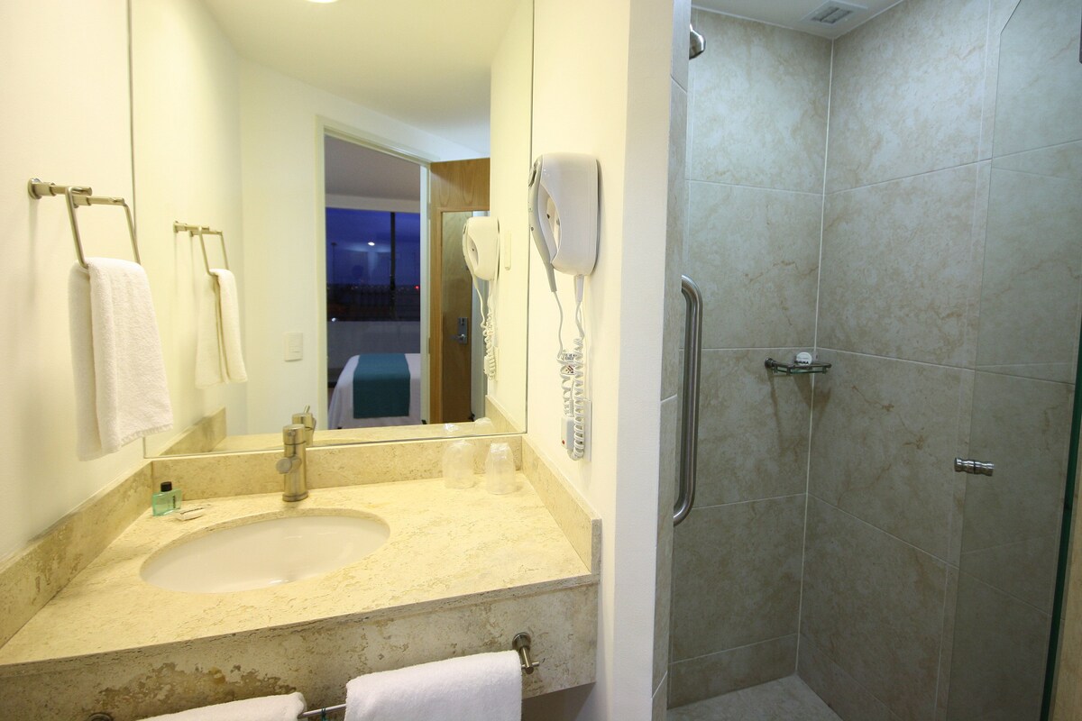 Casa de banho com lavatório, espelho, porta-toalhas, secador de cabelo e chuveiro.