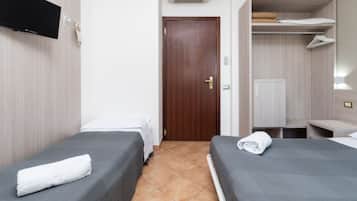 Quarto de hotel com duas camas de solteiro, um guarda-roupa, uma escrivaninha e uma televisão.