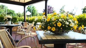 Uma área externa com mesas e cadeiras de vime, e um centro de mesa com flores.