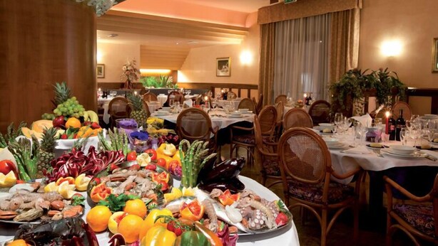 Restaurante com uma mesa de jantar grande e redonda posta para uma refeição, rodeada por cadeiras.