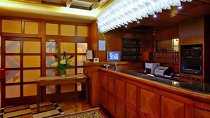 Uma área de recepção com balcão de madeira, piso xadrez, tapete vermelho e parede com painéis de vidro estampado.