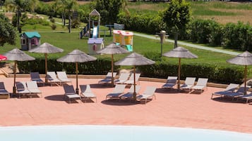 Área da piscina com espreguiçadeiras e guarda-sóis, cercada por vegetação e uma vista deslumbrante da água.