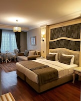 Quarto de hotel com uma cama grande, um espaço de estar com uma poltrona e mesa, e um painel decorativo na parede.