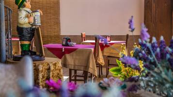 Restaurante com mesas cobertas por toalhas vermelhas, uma estátua de um homem segurando uma caneca de cerveja e diversos flores em primeiro plano.