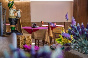 Restaurante com mesas cobertas por toalhas vermelhas, uma estátua de um homem segurando uma caneca de cerveja e diversos flores em primeiro plano.