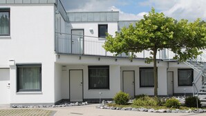 Um edifício moderno com telhado plano, várias portas e uma árvore no pátio.