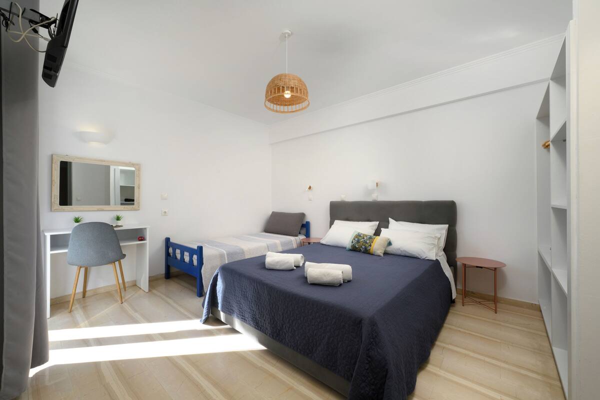 Quarto com cama, escrivaninha, cadeira, mesinha e luminária pendente.