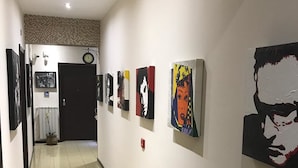 Um corredor com piso ladrilhado e paredes brancas. Várias obras de arte emolduradas estão expostas nas paredes.
