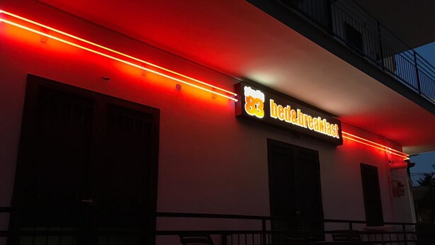 Um edifício com um letreiro de neon que diz 'bed&breakfast' e uma varanda com cadeiras.