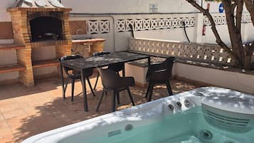 Um pátio com banheira de hidromassagem, forno de tijolos e uma mesa com cadeiras.