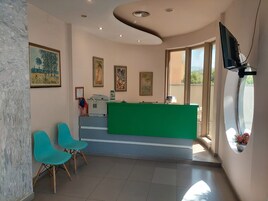 Uma área de recepção com uma mesa verde, duas cadeiras turquesa e uma TV de tela plana fixada na parede.