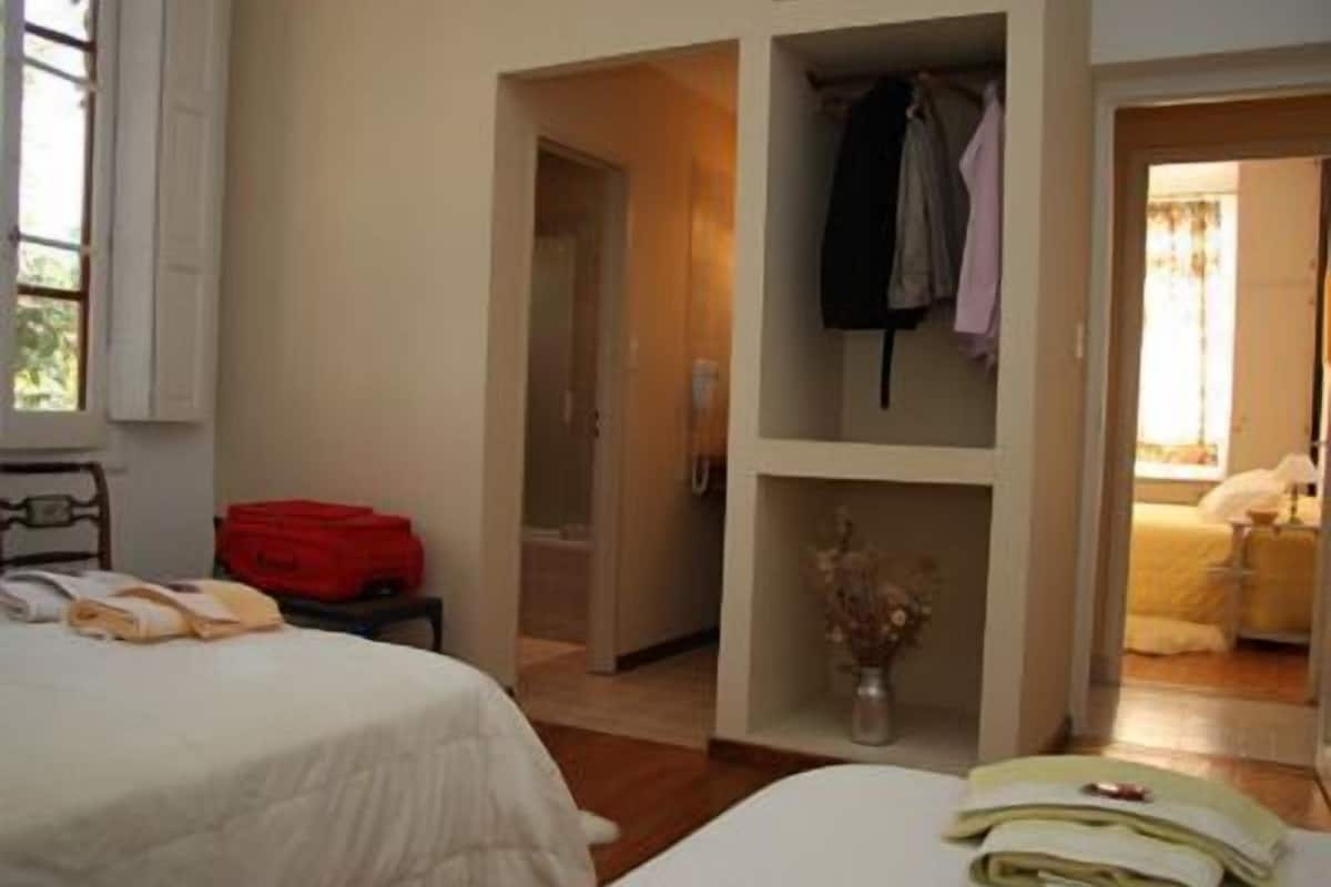 Quarto com duas camas, um guarda-roupa e um banheiro visível através de uma porta aberta.