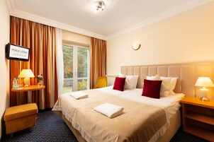 Quarto de hotel com uma cama grande, duas mesas de cabeceira, uma TV e uma janela com cortinas.