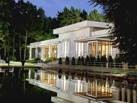 Uma casa moderna de dois andares com grandes janelas e uma piscina refletora na frente.
