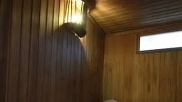 Uma sala de sauna de madeira com um banco, uma mesa pequena e uma janela que proporciona luz natural.