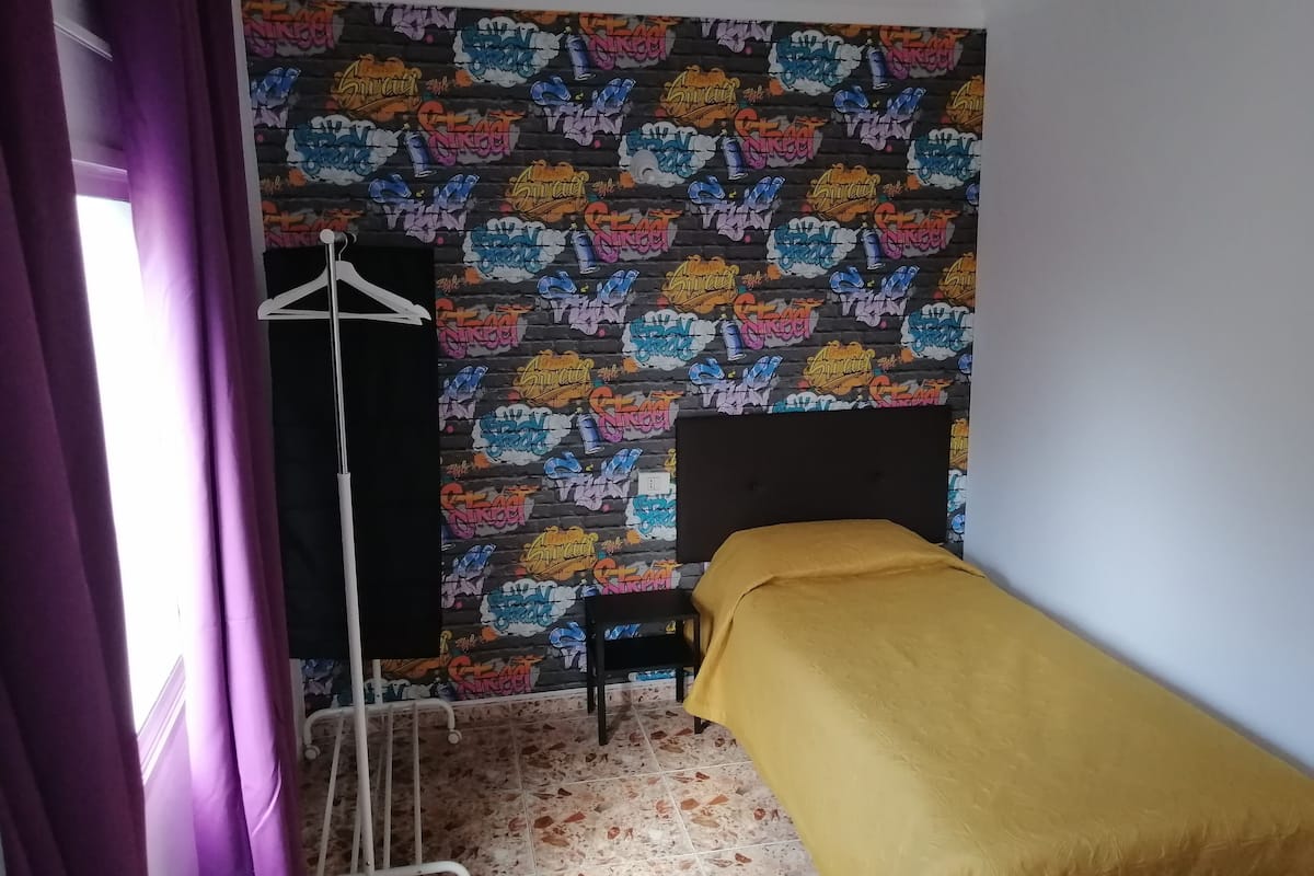 Quarto pequeno com uma cama, um guarda-roupa e uma parede coberta por arte de graffiti.