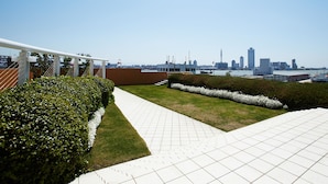 Terraço no telhado com vista clara para o horizonte urbano, caminho de azulejos e sebes bem aparadas.