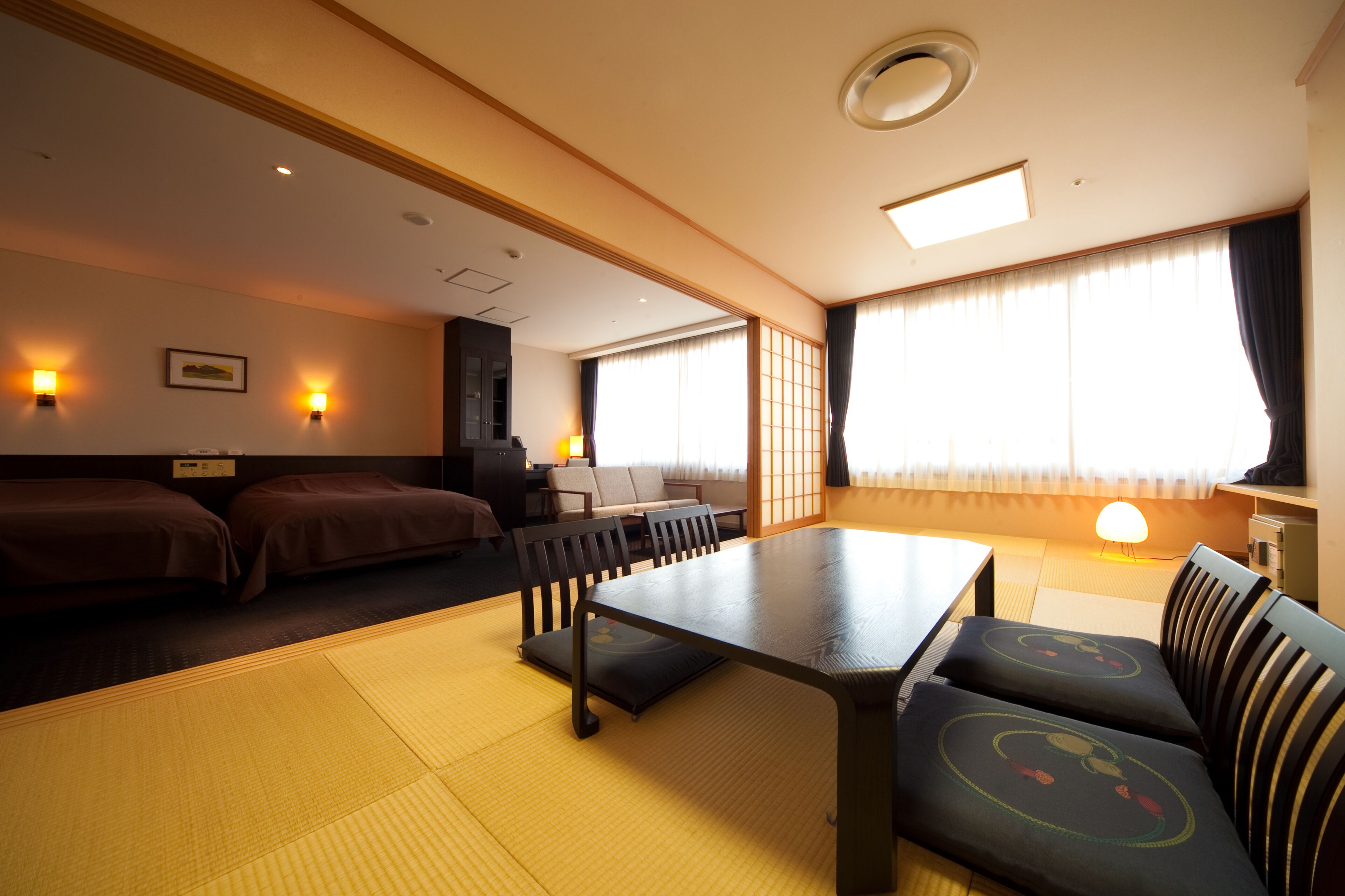 Quarto de hotel com chão de esteira de tatame, uma mesinha, dois sofás, uma escrivaninha e uma cama.