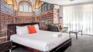 Quarto de hotel com uma cama grande, uma escrivaninha, uma cadeira e um mural de estante na parede.