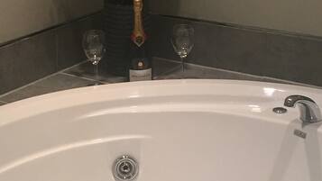 Uma banheira grande e branca com um ralo, uma garrafa de champanhe e duas taças de vinho sobre uma superfície revestida de azulejos.