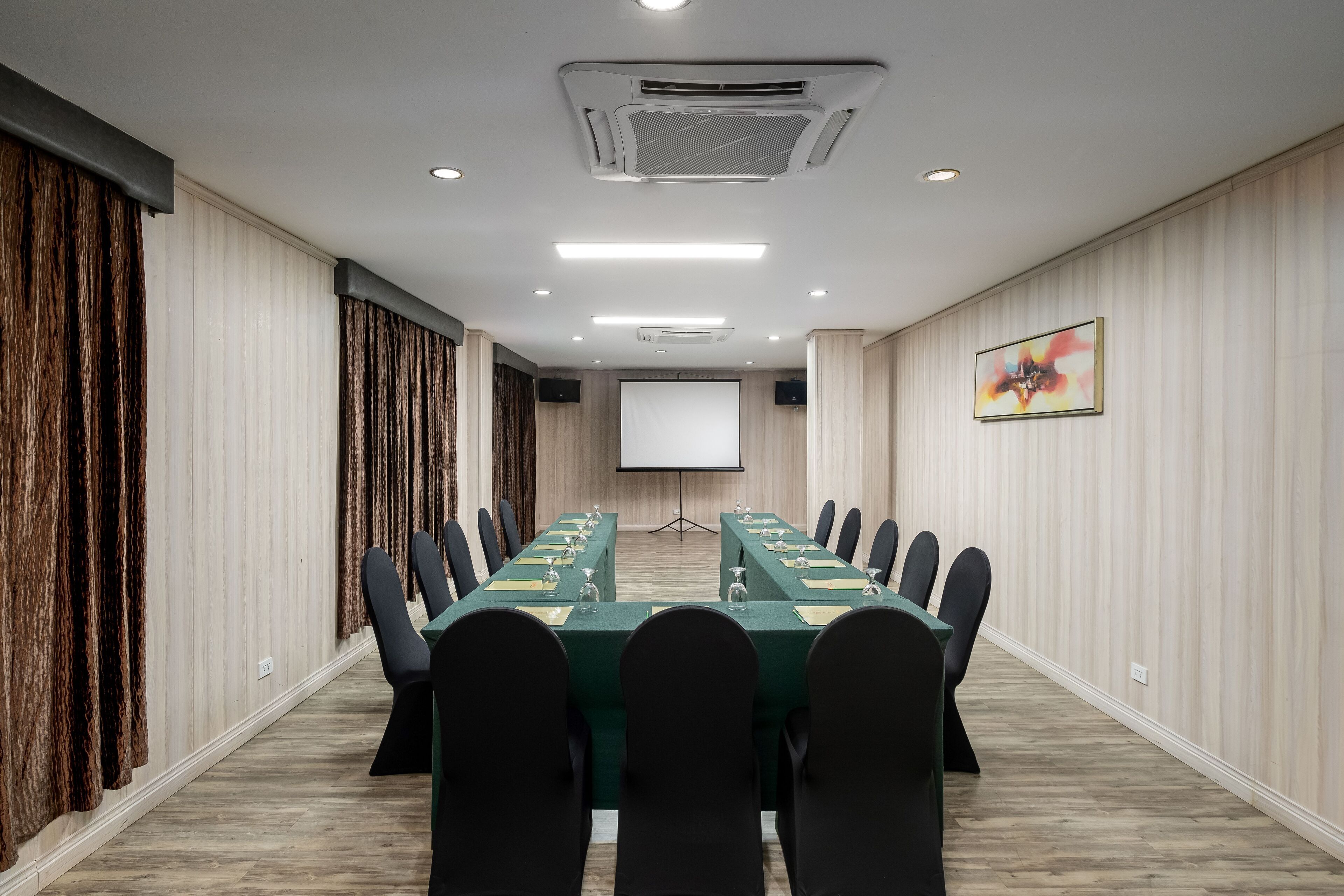 Sala de conferências com uma mesa comprida, cadeiras pretas e tela de projeção.