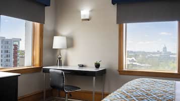 Quarto de hotel com escrivaninha, cadeira, luminária e cama com colcha estampada.