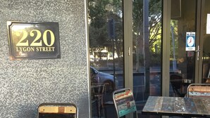 Mobiliário de exterior com cadeiras de metal e mesas de madeira, um vaso com flores e uma placa com o endereço 220 Lygon Street.