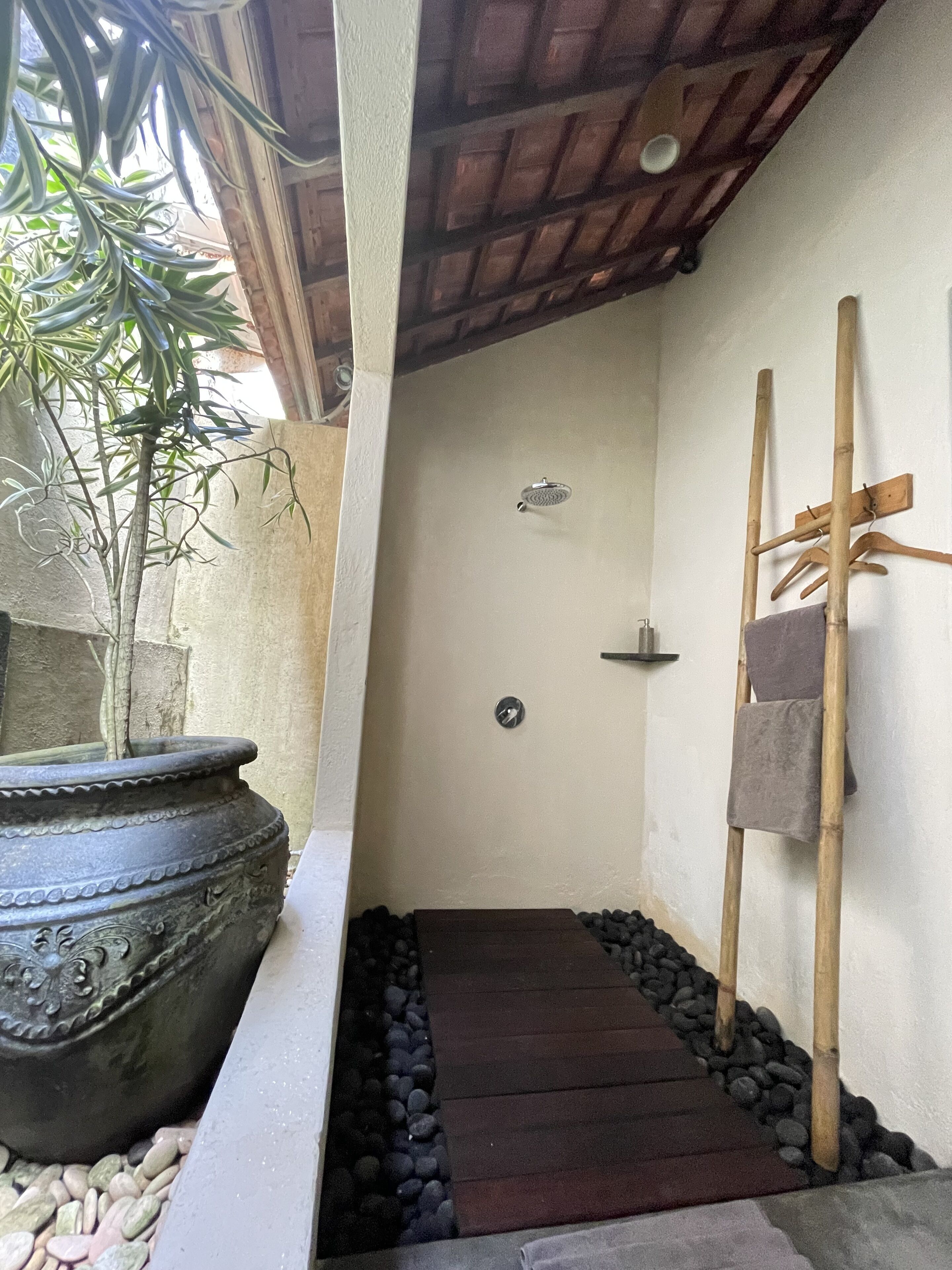 Um espaço ao ar livre pequeno e cercado, com um caminho de pedra que leva a uma porta, delimitado por um muro de pedra baixo e um vaso grande com planta.