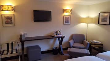 Quarto de hotel com cama, escrivaninha, cadeira, televisão e abajur.