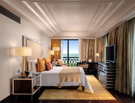 Quarto de hotel com uma cama grande, duas mesas de cabeceira, uma escrivaninha com cadeira, televisão e varanda com cortinas.