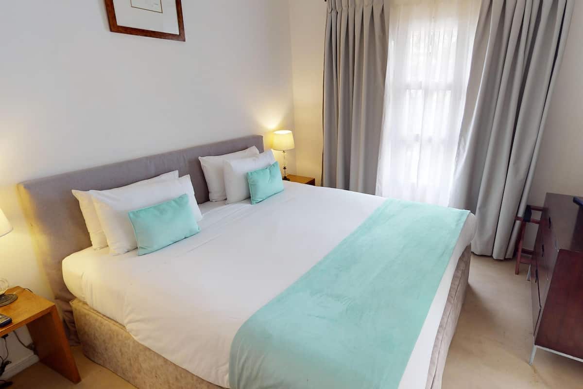 Quarto de hotel com uma cama grande, uma televisão sobre um suporte de madeira e uma janela com cortinas.