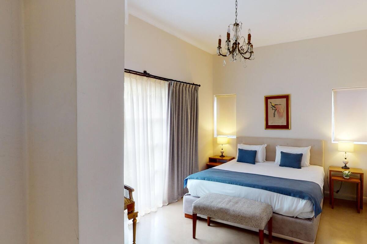Quarto com uma cama grande, duas mesas de cabeceira com luminárias, um candelabro, uma janela com cortinas e um quadro na parede.