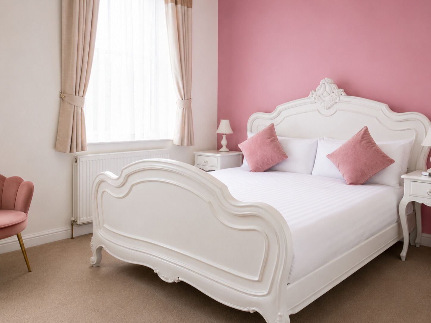 Quarto com uma cama branca e detalhada, almofadas cor-de-rosa, mesa de cabeceira branca, cadeira cor-de-rosa e uma janela com cortinas.