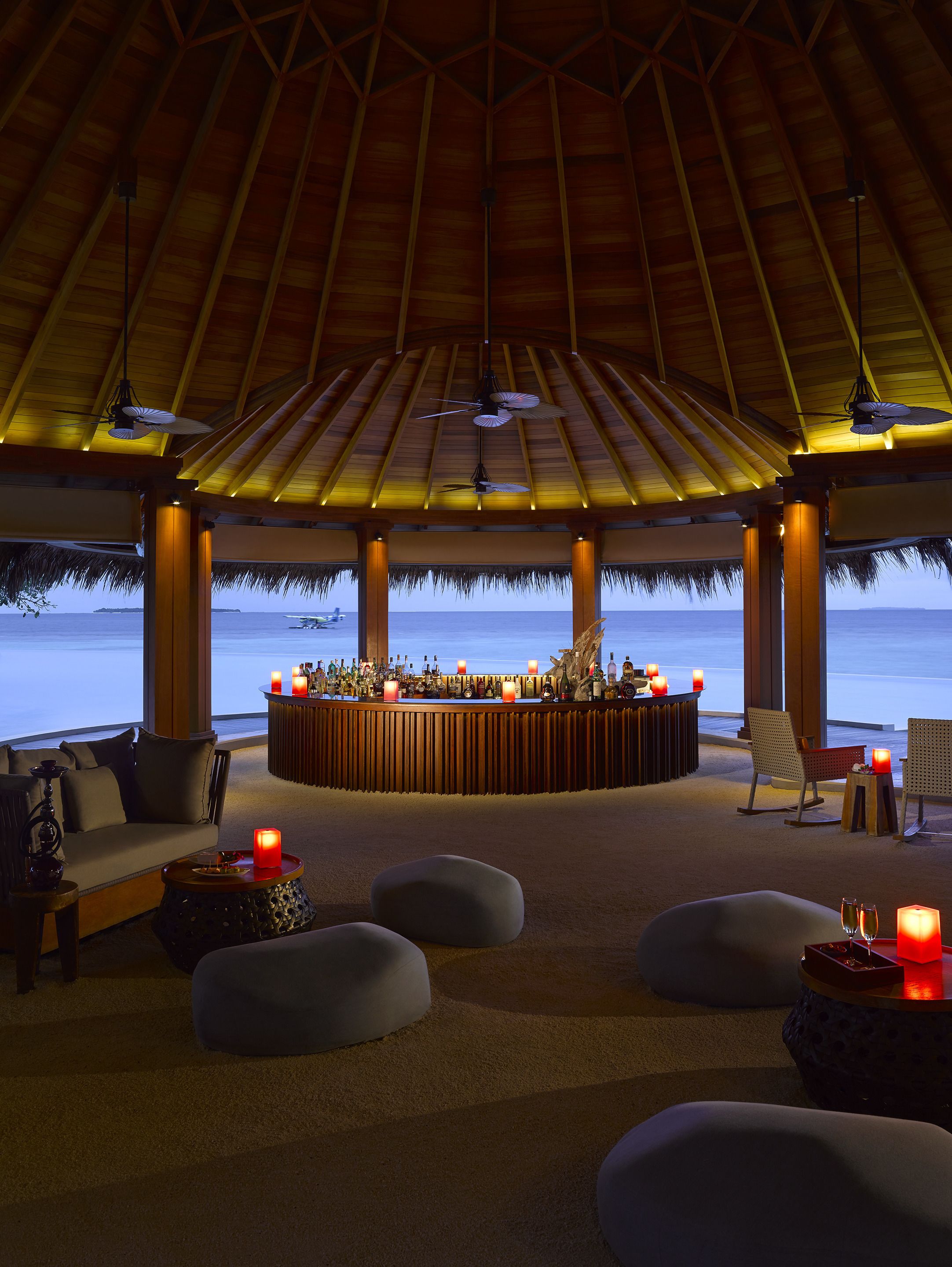 Um espaço de relaxamento à beira-mar com teto de palha, bar com velas e áreas de estar.
