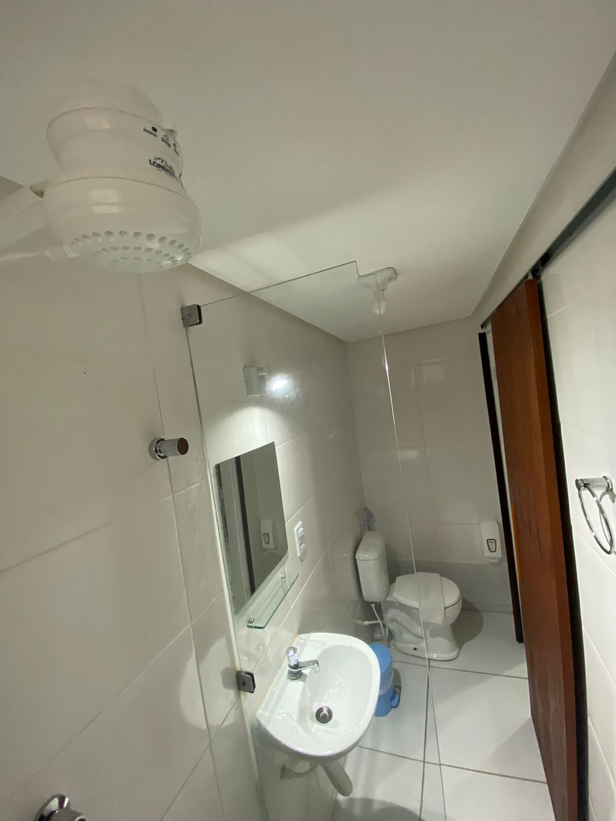 Uma casa de banho moderna com chuveiro envolto em vidro, uma sanita e uma pia branca com espelho.