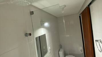 Uma casa de banho moderna com chuveiro envolto em vidro, uma sanita e uma pia branca com espelho.