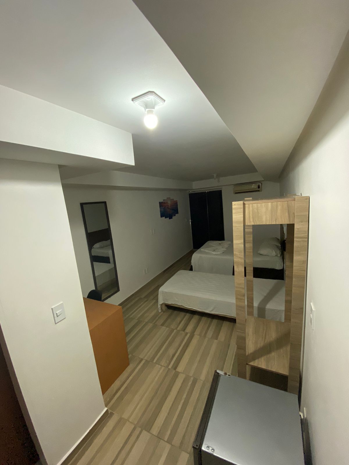 Quarto pequeno com cama beliche, escrivaninha e espelho.