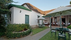Um edifício com telhado verde, área externa com mesas e cadeiras, e um caminho que leva à entrada.