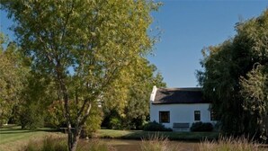 Uma casa branca com telhado preto, cercada por vegetação exuberante e um pequeno lago.