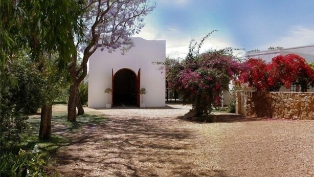 Um edifício com fachada branca, entrada em arco e caminho de cascalho que o leva até ele.