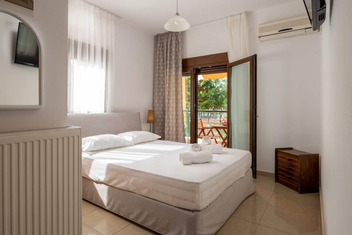 Quarto com cama, radiador, televisão e janela com cortinas.