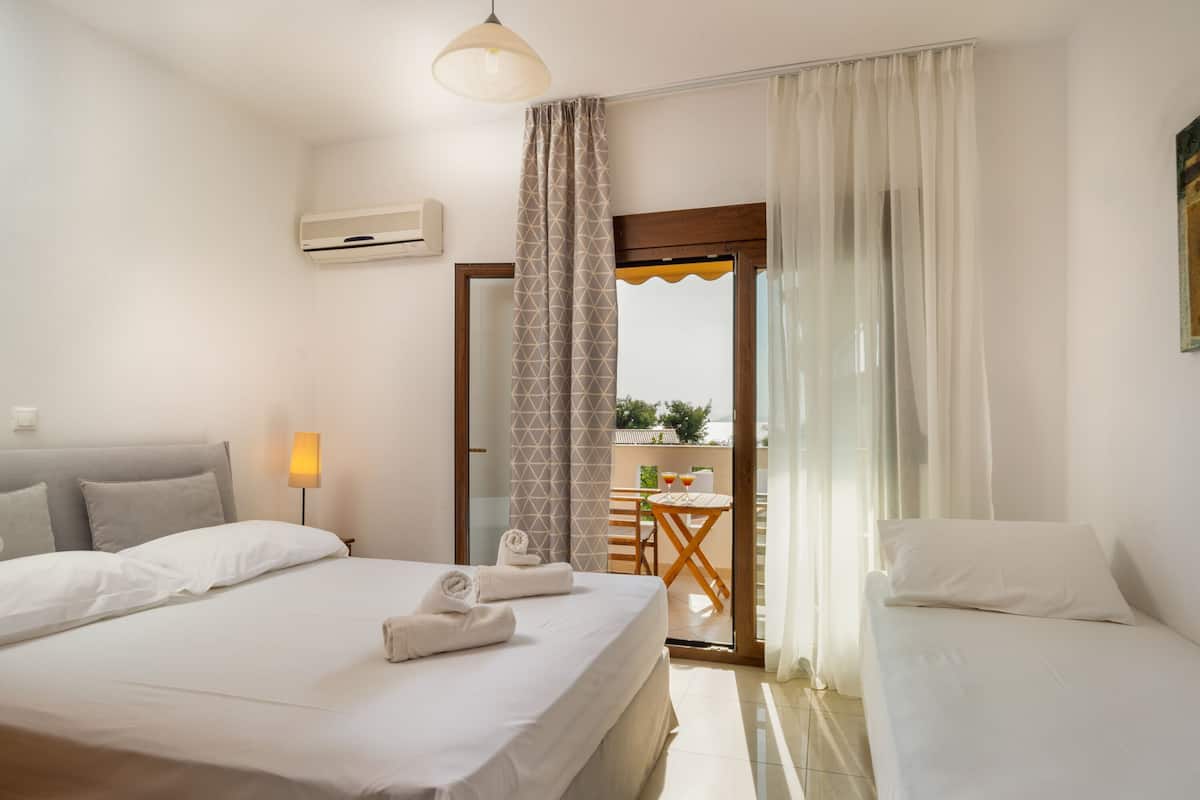 Quarto de hotel com cama, sofá, mesa com cadeiras e varanda com mesa e cadeiras.