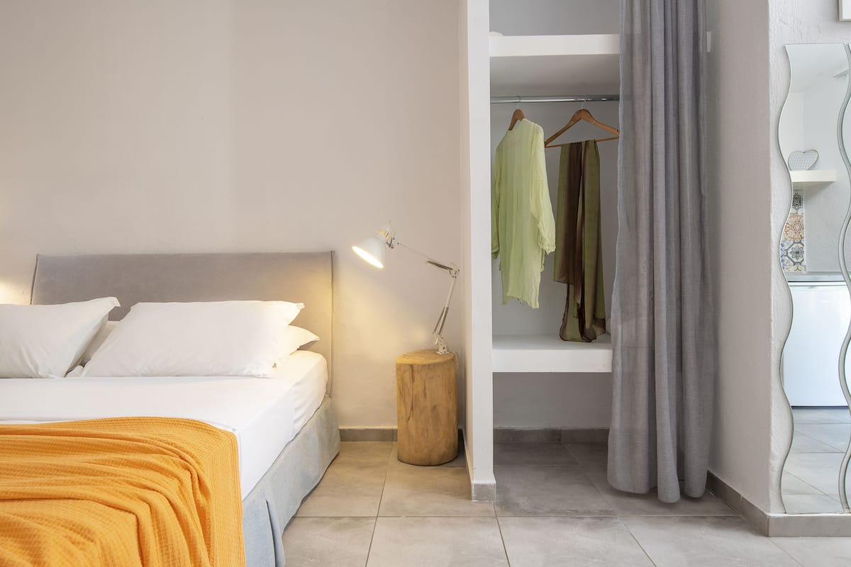 Quarto bem arrumado com cama, abajur e um pequeno banquinho de madeira.