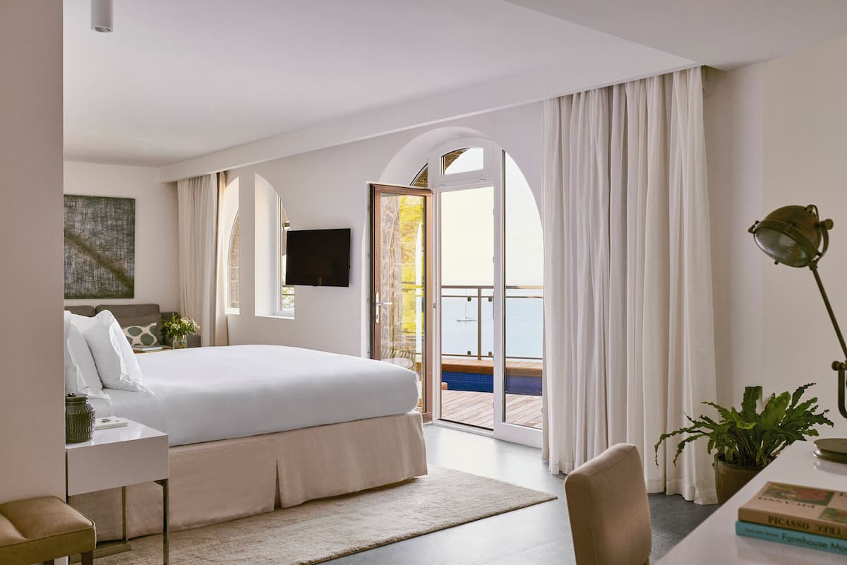 Quarto de hotel moderno com uma cama grande, uma mesa de escritório, TV e vista para a piscina e área externa.