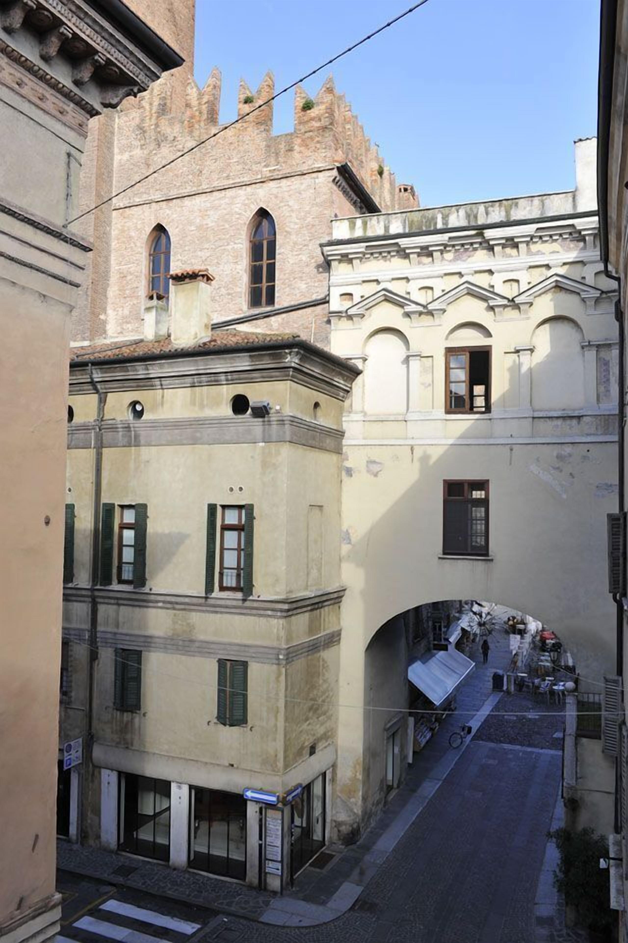 Uma rua estreita com edifícios históricos, incluindo uma torre imponente e um edifício com um arco.