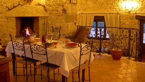 Uma área de jantar com paredes de pedra, lareira e uma mesa posta para dois.