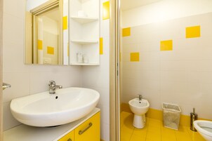 Uma casa de banho com uma pia branca, armários amarelos, um bidé e um cesto de lixo.