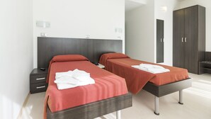 Quarto de hotel com duas camas de solteiro, cabeceira de madeira escura, mesa de cabeceira pequena, guarda-roupa e ar-condicionado instalado no teto.