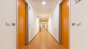 Um corredor comprido e estreito, com paredes laranja e chão branco, que leva a uma porta no final.